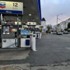 A series of gas station pumps stand unused in the foreground of a dark, dusky sky.